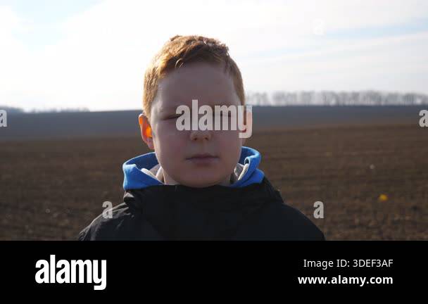 Serious red-haired boy looks into camera against the blurred background ...