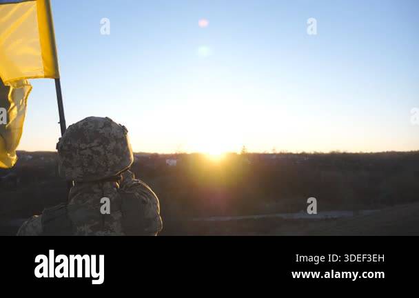 Ukrainian army man stands at the peak of hill waving blue-yellow banner ...