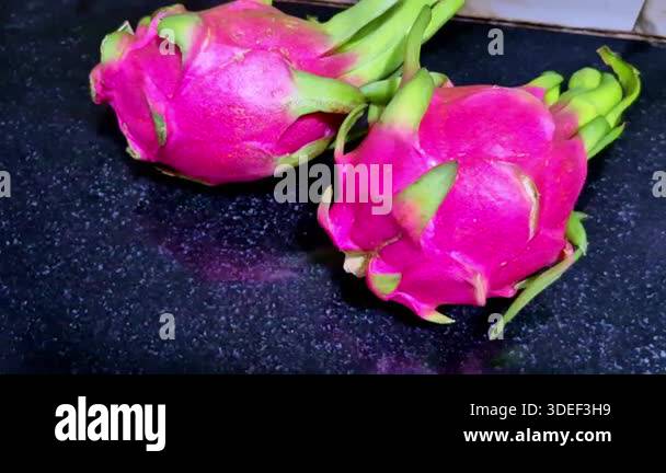 A close-up of two fresh dragon fruits resting on a dark surface ...