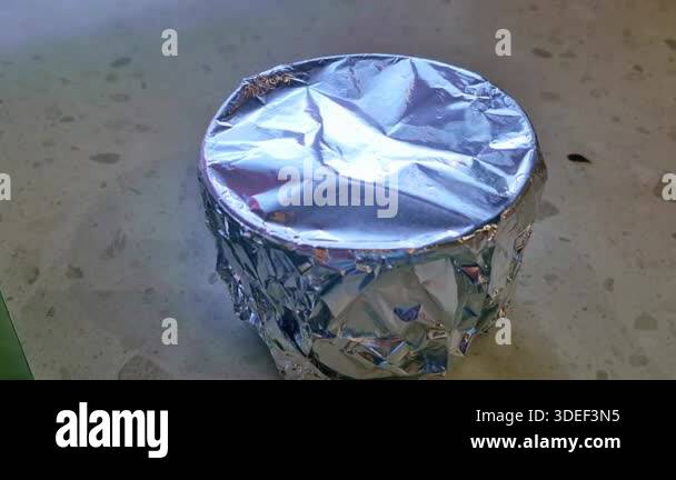 A small cylindrical container wrapped tightly in crinkled aluminum foil ...