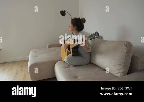 Woman plays acoustic guitar at home on sofa. Girl plays musical ...