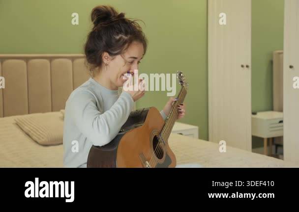 Woman plays acoustic guitar in bedroom and smiles. Practicing and ...