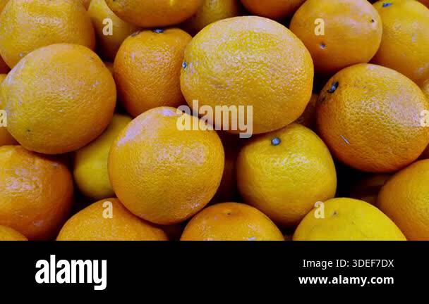 A close-up of fresh oranges piled together at a market stall, showing ...