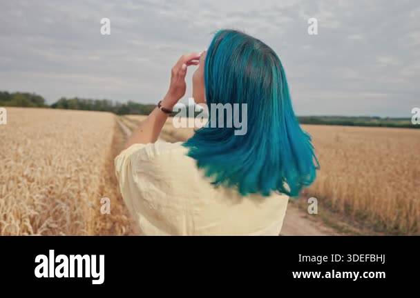 Unique woman standing in golden wheat field, gently tossing turquoise ...