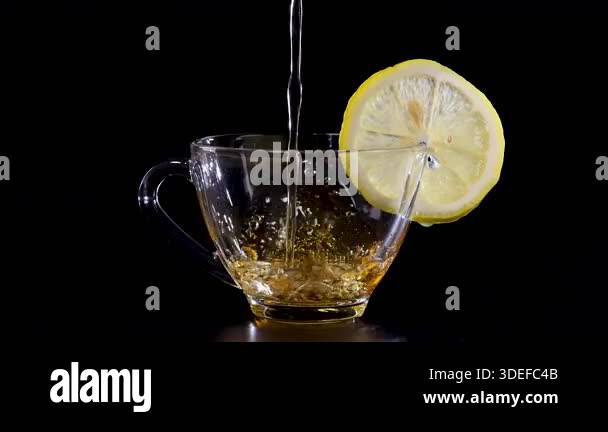 Glass cup with lemon slice filled with tea against a black backdrop ...