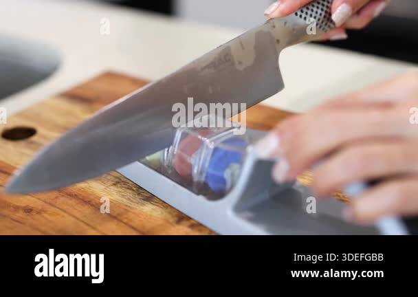 Hands sharpening a knife on a stone in a well-lit kitchen environment ...