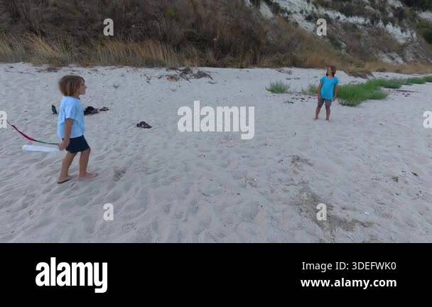 Two children playing catch on sandy beach near sea cliffs. Carefree ...