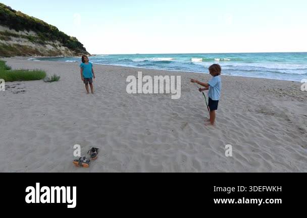Two children playing catch on sandy beach near sea cliffs. Carefree ...