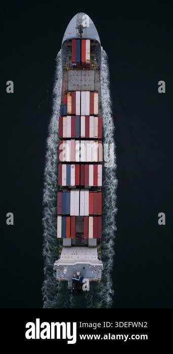 Top-down aerial view of container ship cutting through dark water ...