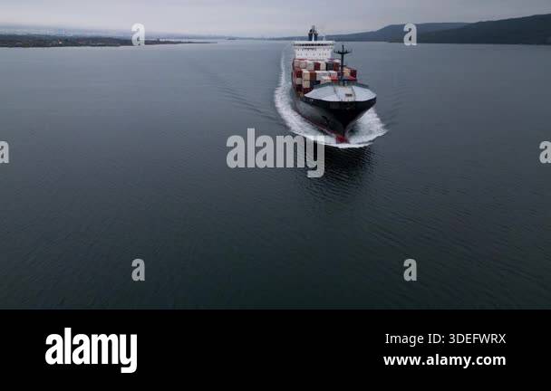 Aerial view of large container ship moving across calm sea, leaving ...
