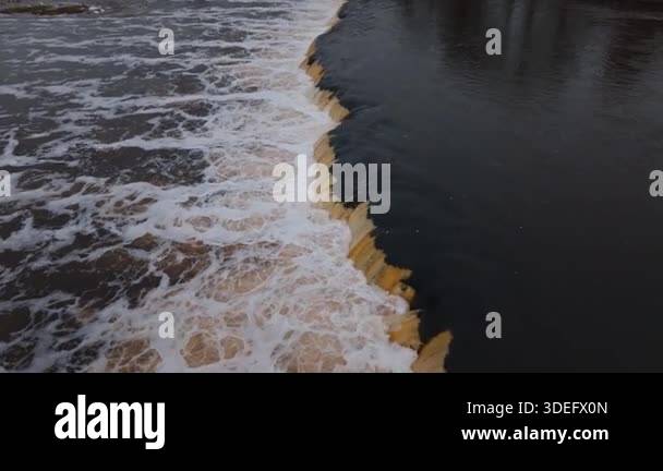 Aerial view of a rural river weir shows water plunging in a diagonal ...