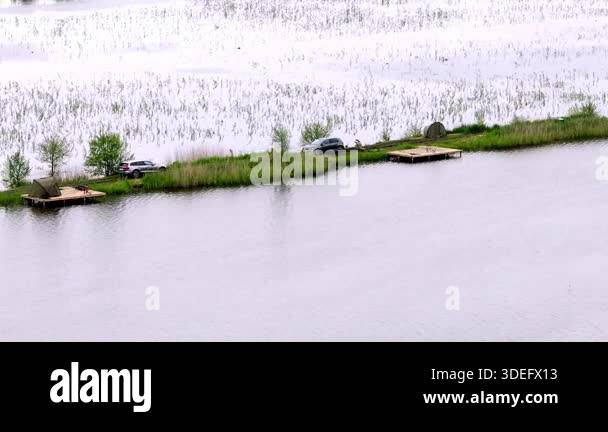 Aerial view of narrow lakeside spit with cars, tents, and platforms ...