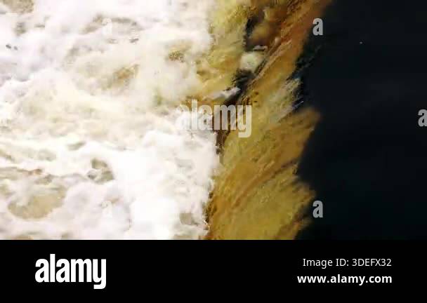 Top down close up of river rushing over low weir into dark pool. White ...
