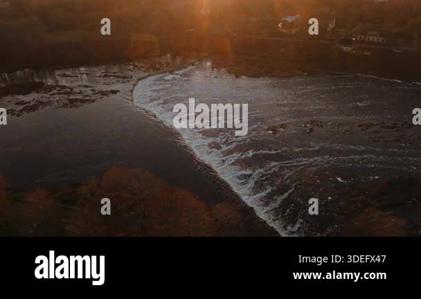 Aerial view of curved stone weir splitting river at sunset. Title in ...