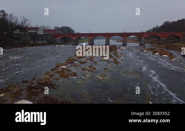 Aerial of Kuldiga red brick arch bridge over Venta River in winter ...
