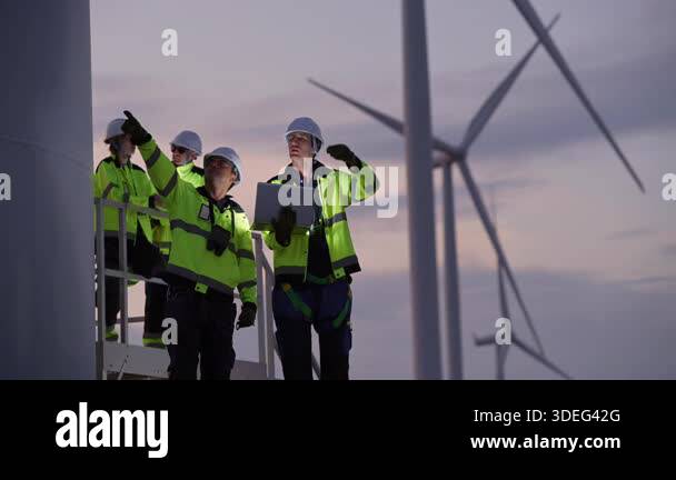 Engineers wearing safety helmets and jackets inspecting a wind turbine ...