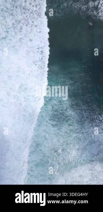 Top-down aerial drone view of an ocean wave breaking into white sea ...