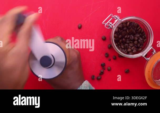 Top view of person's hands grinding roasted coffee beans on red ...