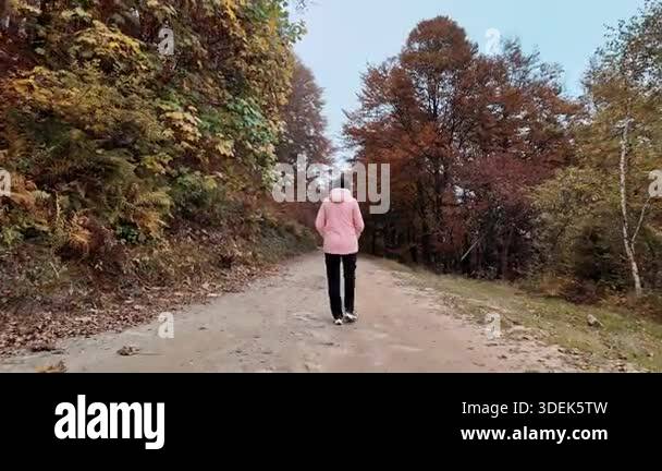 Woman in pink jacket walking on autumn road in Italian alpine nature ...
