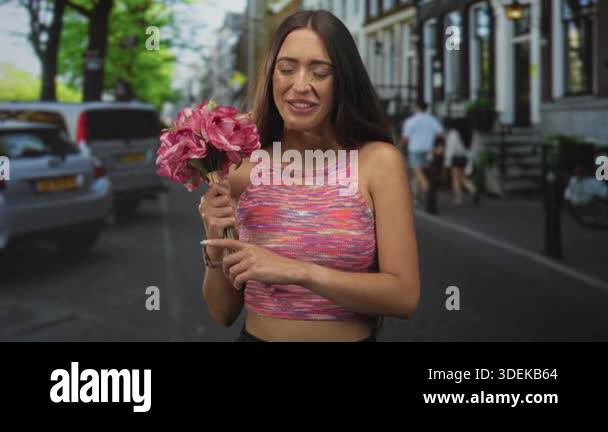 Woman holding a bouquet and smelling flowers on street with closed eyes ...