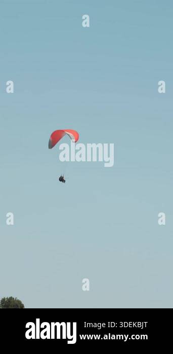 Red parachute flying against clear blue sky. Parasailing in sea across ...