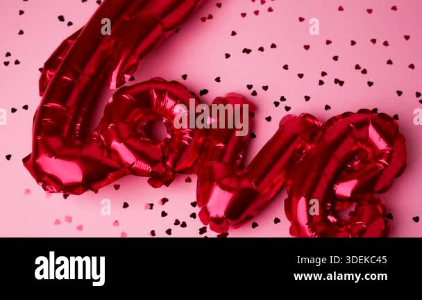 Red foil LOVE balloons and heart confetti on pink for a romantic ...