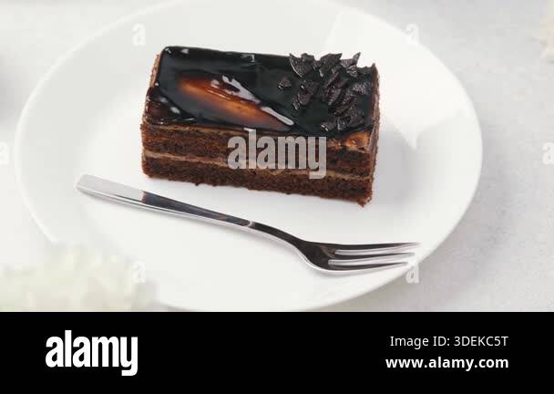 Rich chocolate cake slice with glossy frosting and dark flakes on white ...
