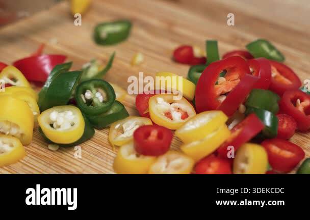 A knife slices through fresh chili peppers on a wooden cutting board ...