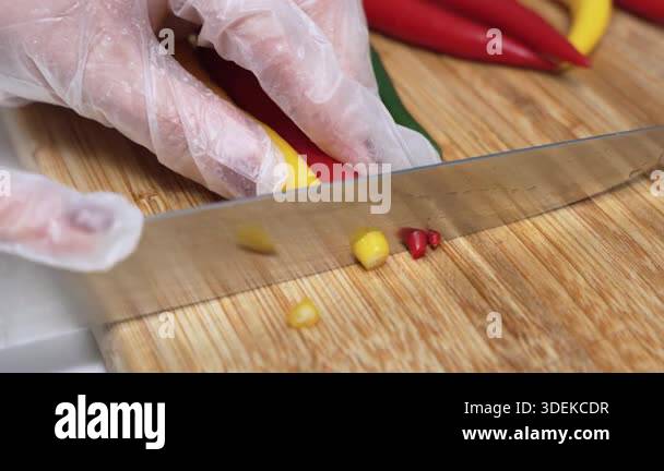 A knife slices fresh chili peppers on a wooden cutting board. The macro ...