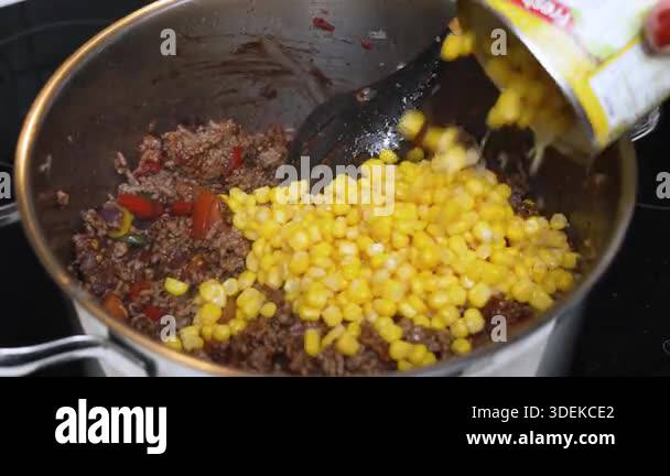 Corn kernels are poured into a simmering pot of chili with minced meat ...