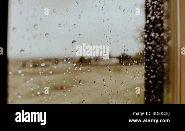 Raindrops on a window with a blurred background of a field and sky. The ...