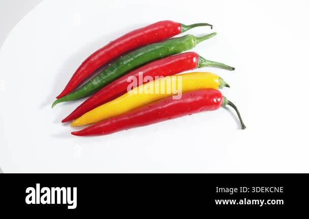 Mixed red, green, and yellow chili peppers rotating on a clean white ...