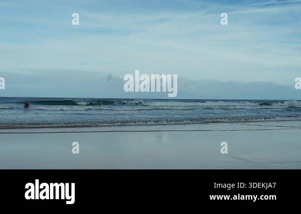 cloudy shoreline with surfers and choppy waves. High quality 4k footage ...