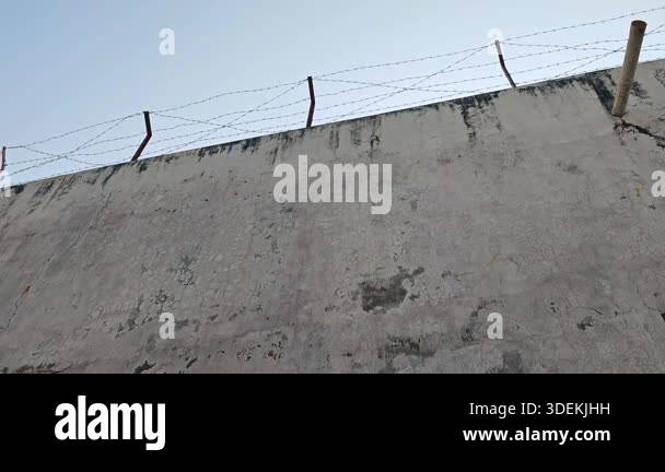A tall, imposing concrete prison wall topped with sharp razor wire ...