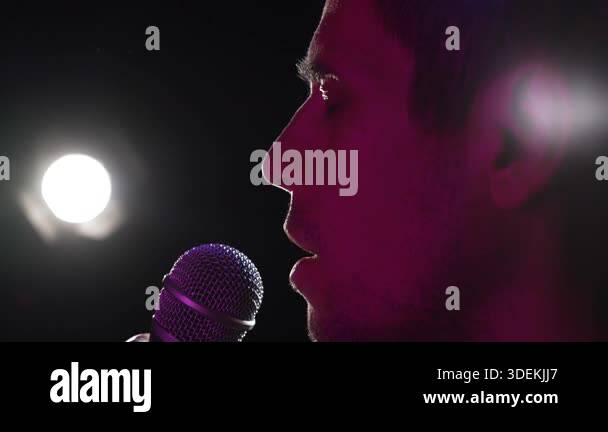 A man stands solo on a quiet stage, singing a gentle acoustic song into ...