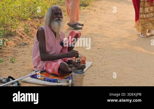 A person, possibly a beggar or devotee, sits on the roadside singing ...