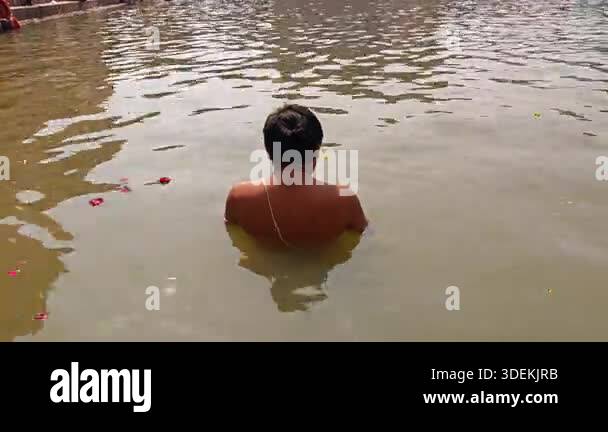 A devotee stands waist-deep in a sacred river like the Ganges, offering ...