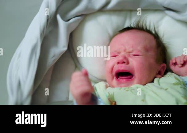 Emotional newborn baby crying with tears in a baby bouncer, showing ...