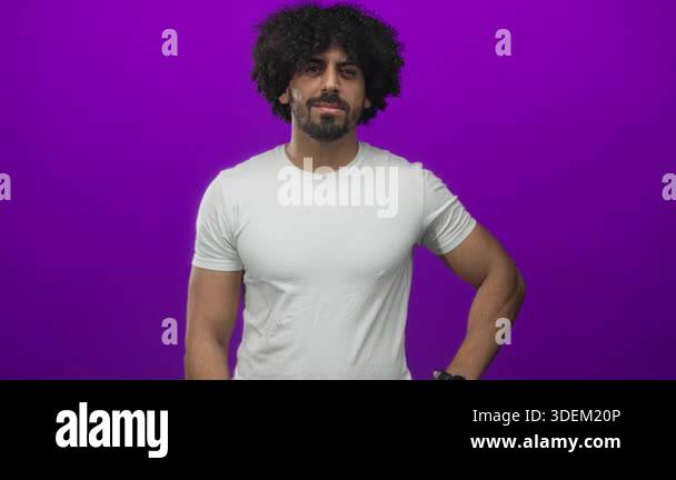 Man pinches nose with hand in purple studio, curly hair and white t ...