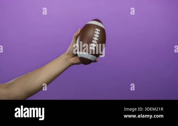 Man holding football in hand against a vibrant purple background ...
