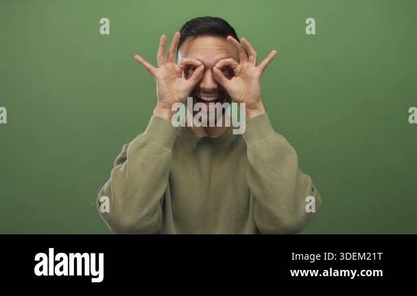 Young hispanic man playfully posing with binoculars gesture against ...