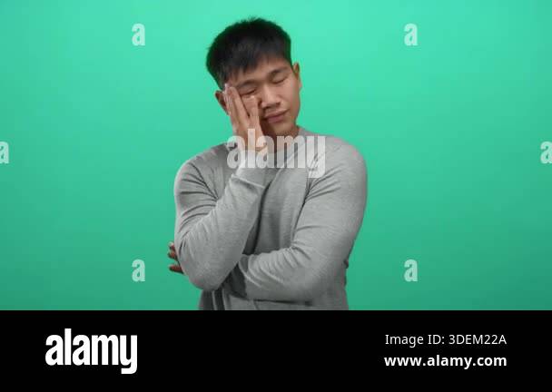 Young man in grey sweater with hand on face over isolated green ...