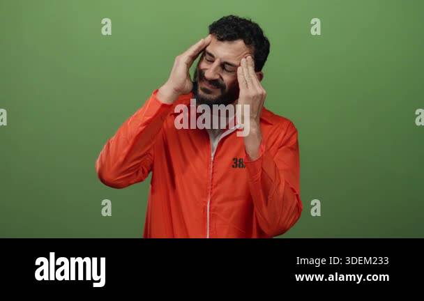 Hispanic man with beard wearing orange jumpsuit stands against green ...