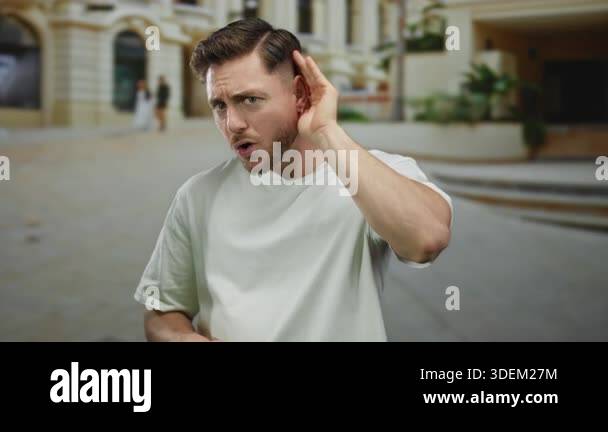 Young man with beard listening intently on city street with blurred ...