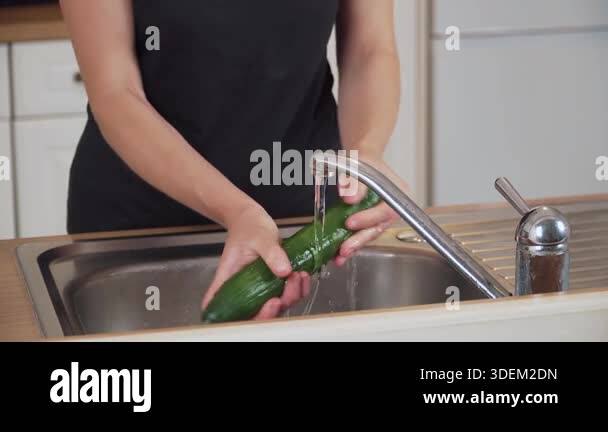 Washing cucumber under running water in sink. Unrecognizable person ...