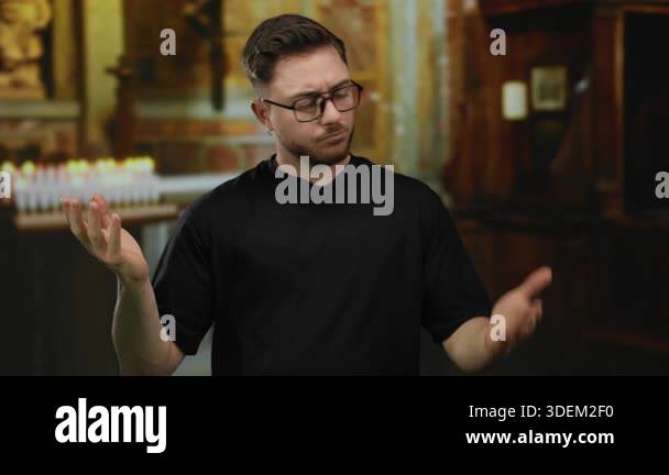 Young man with beard and glasses stands indoors in a church setting ...
