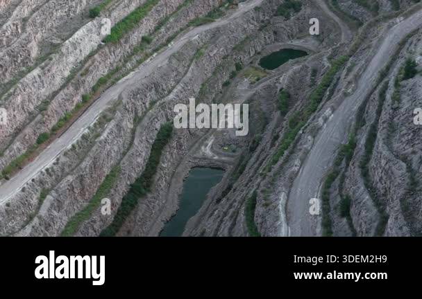 Terraced quarry basin enclosing green water pools and active extraction ...