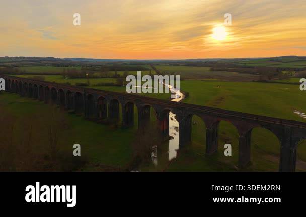Historic railway viaduct crossing serene valley under golden sunset ...