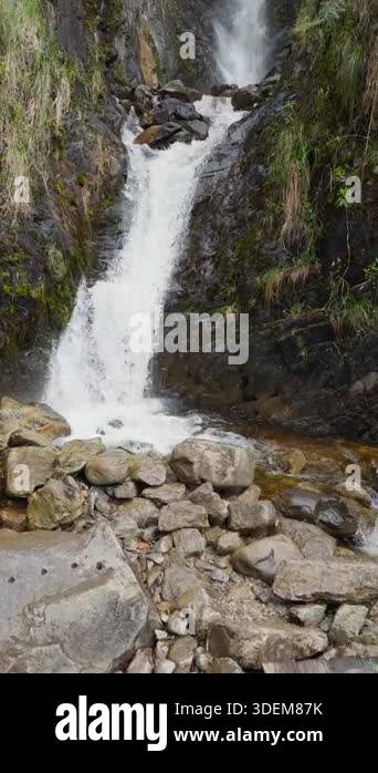A vertical pan up showing a tall narrow waterfall cascading over dark ...