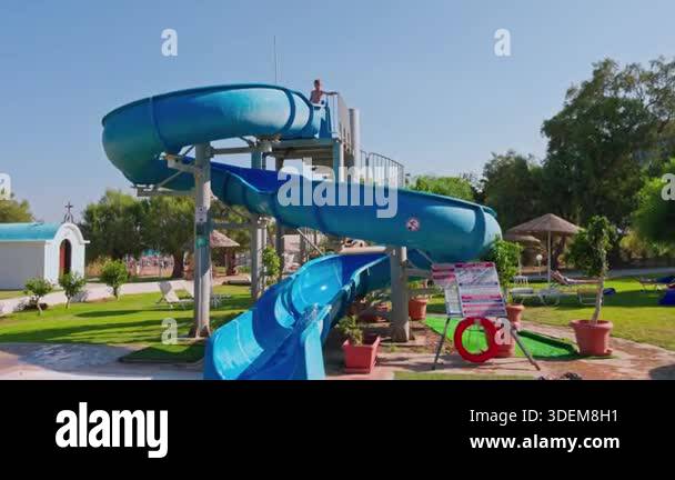 Children sliding down blue water slide into swimming pool at resort ...